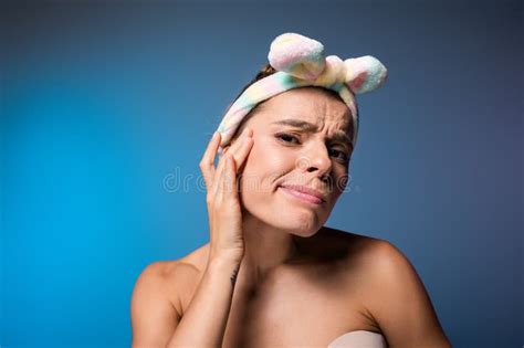 Young Woman Wearing a Colorful Headband Examines Her Face with Concern Against a Blue Gradient ...